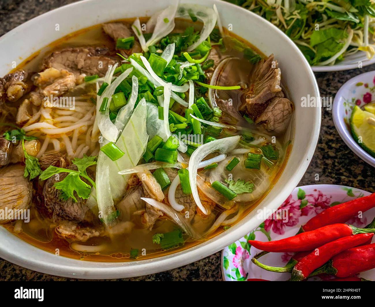 Vietnamese Bun bo food served in a white bowl with red chili peppers on ...