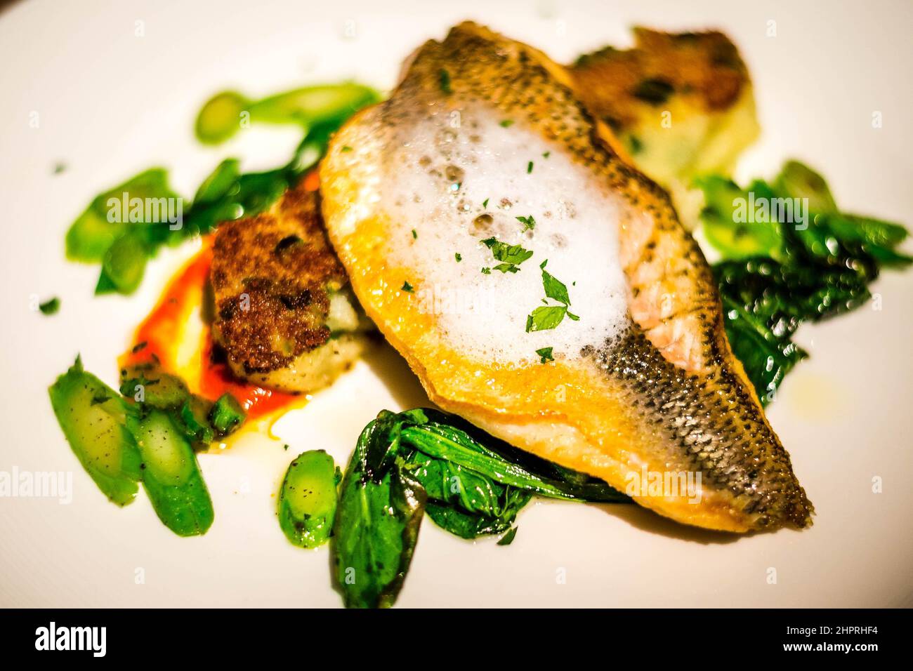 Grilled seabass fish with gin mare foam and vegetables on a white plate ...