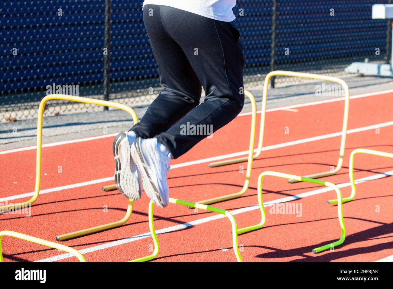 A track and field runner in white shoes jumping over small plastic ...