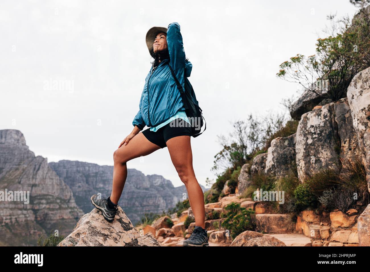 Smiling woman hiker in sports clothes holding a hat on her head while ...