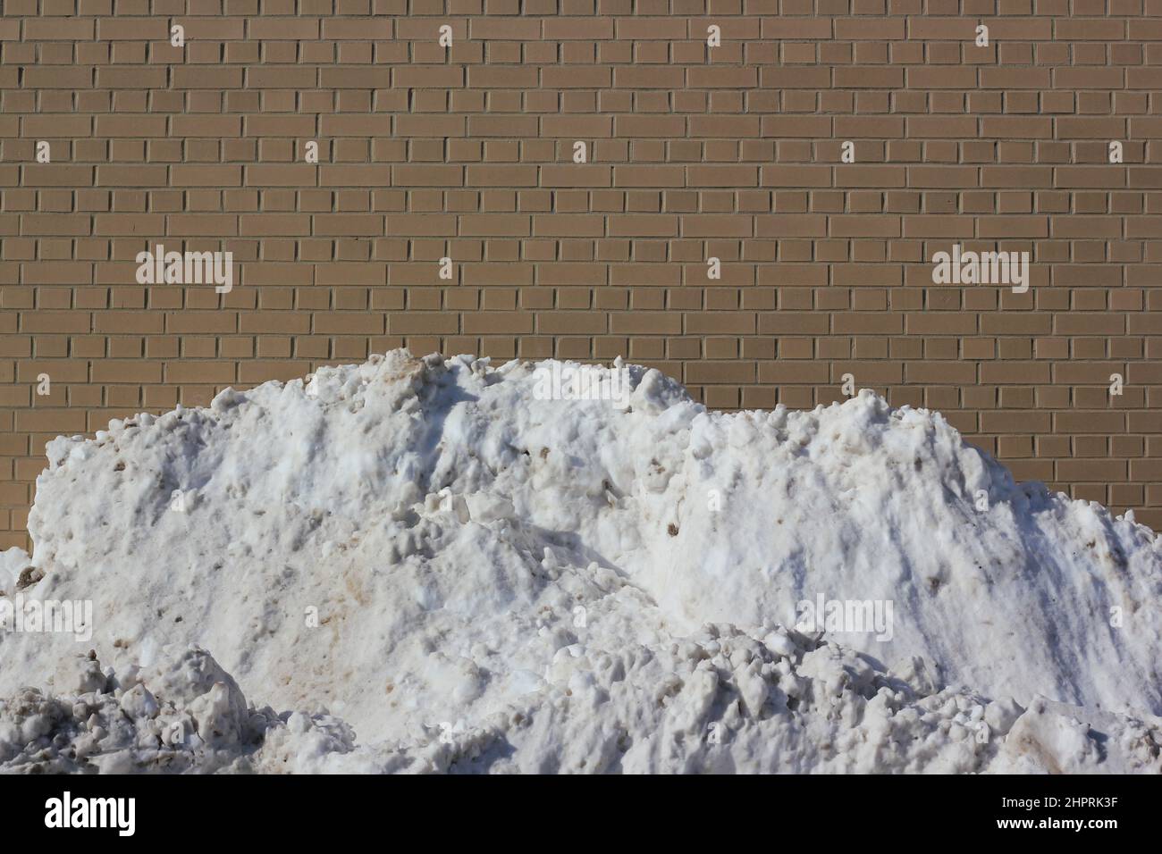 A huge pile of snow against a beige common brick wall, a typical scene ...