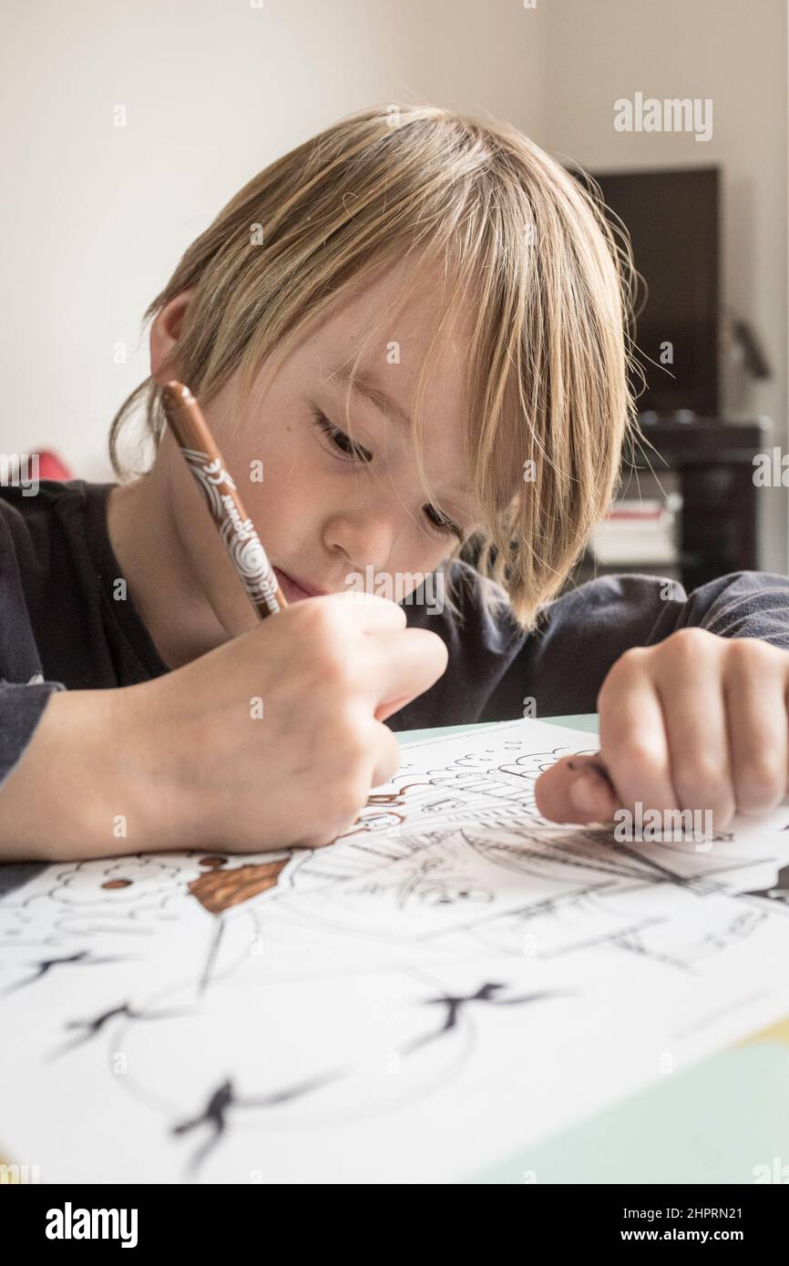 A close up of a small blonde boy focused on coloring with his pens ...