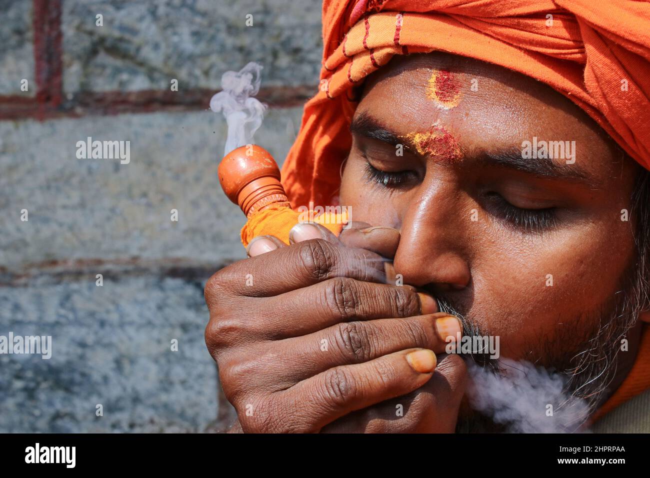 A sadhu, devotee of Lord Shiva smokes marijuana from a pipe made upof ...
