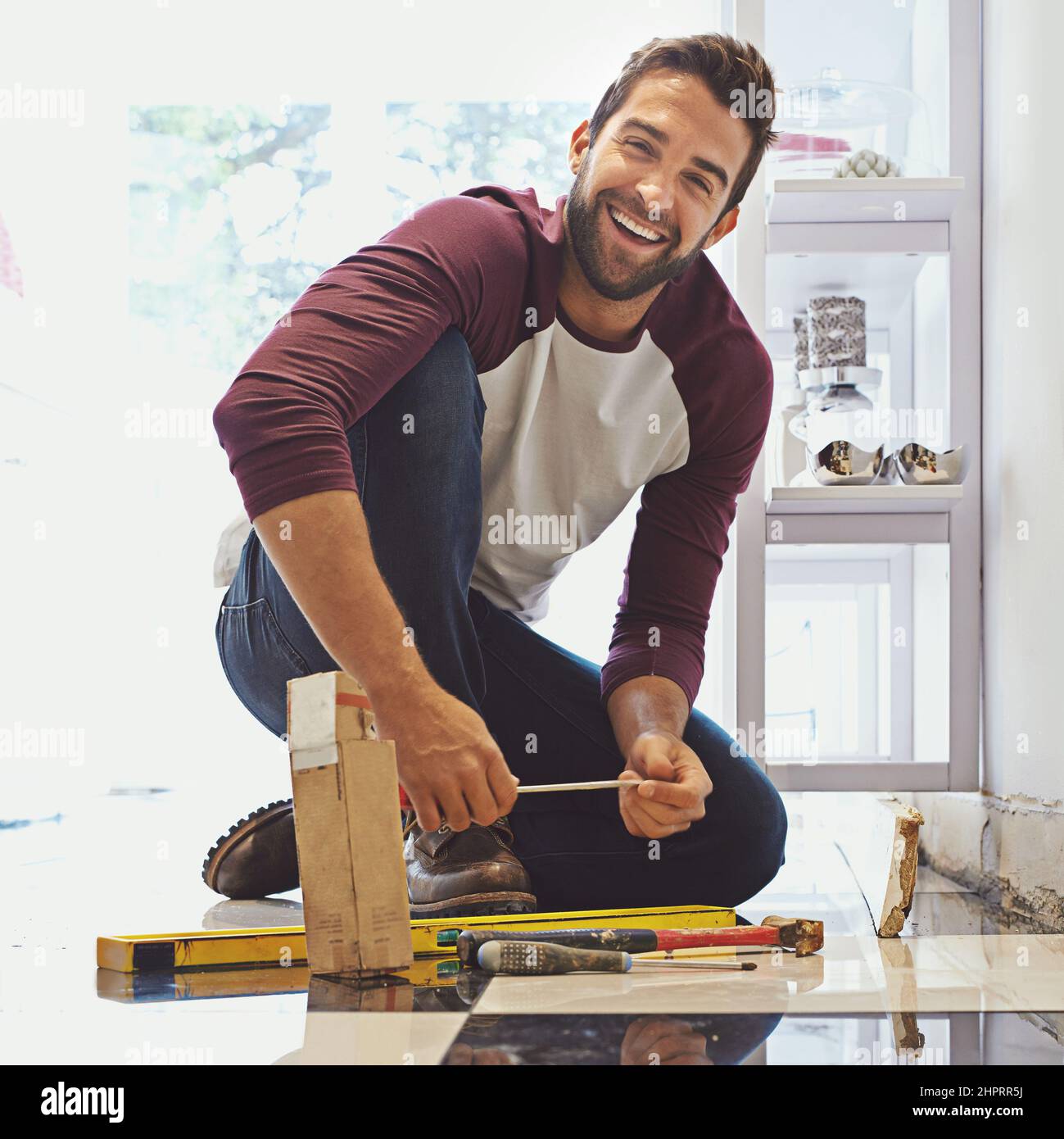 Decorating one tile at a time. Portrait of a smiling man laying floor ...