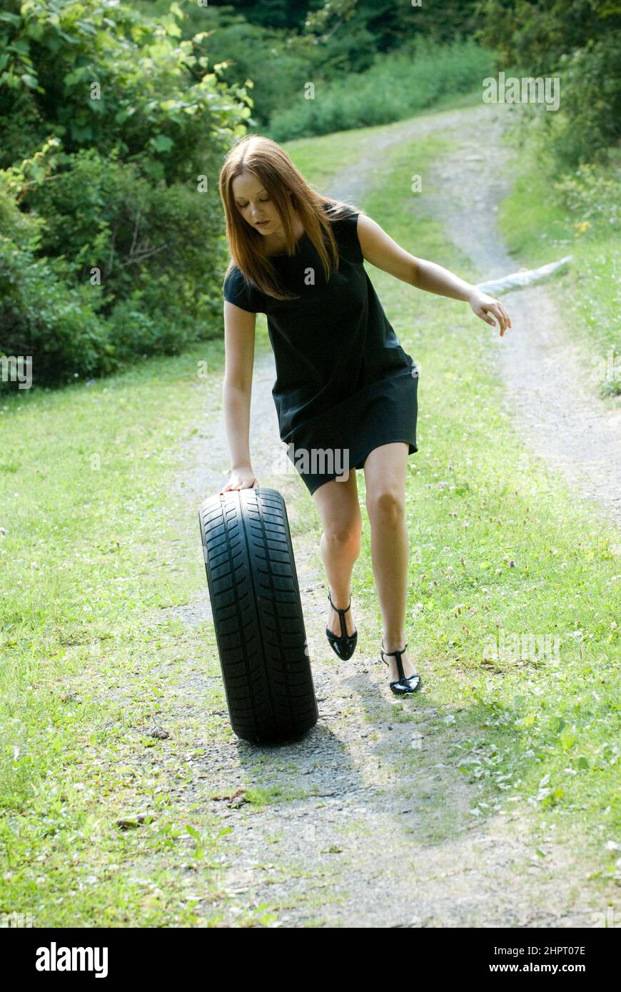 Young woman pushing a car tire down the hill Stock Photo - Alamy