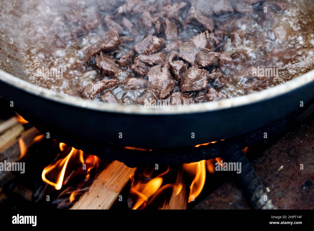Pieces of meat for pilaf are stewed in cauldron over bonfire Stock ...