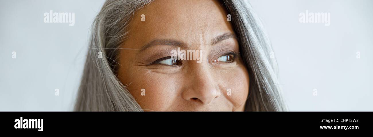 Asian lady with loose grey hair poses for camera on light background ...