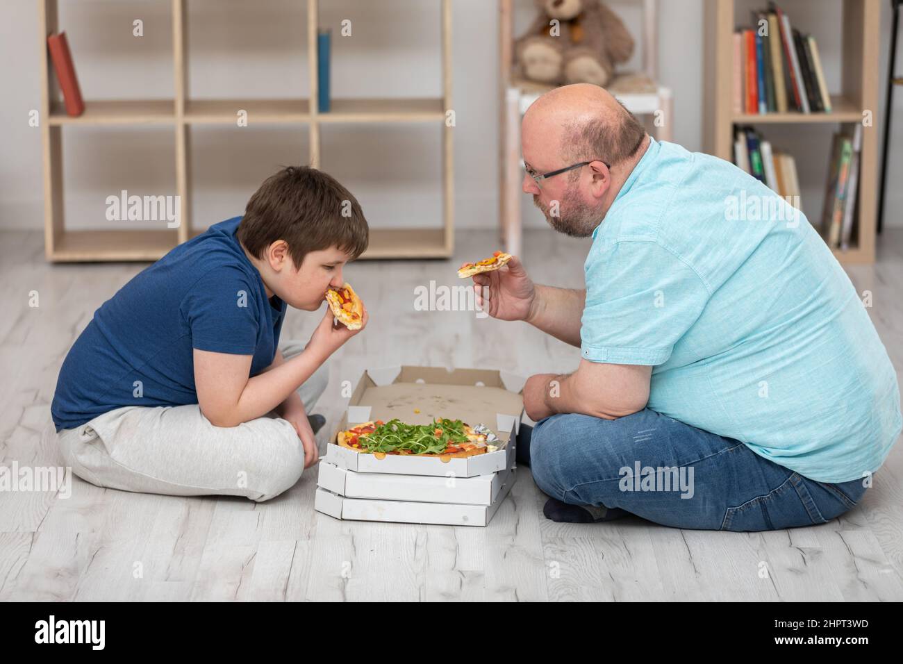Dad and son are sitting on the floor eating fresh pizza Stock Photo - Alamy