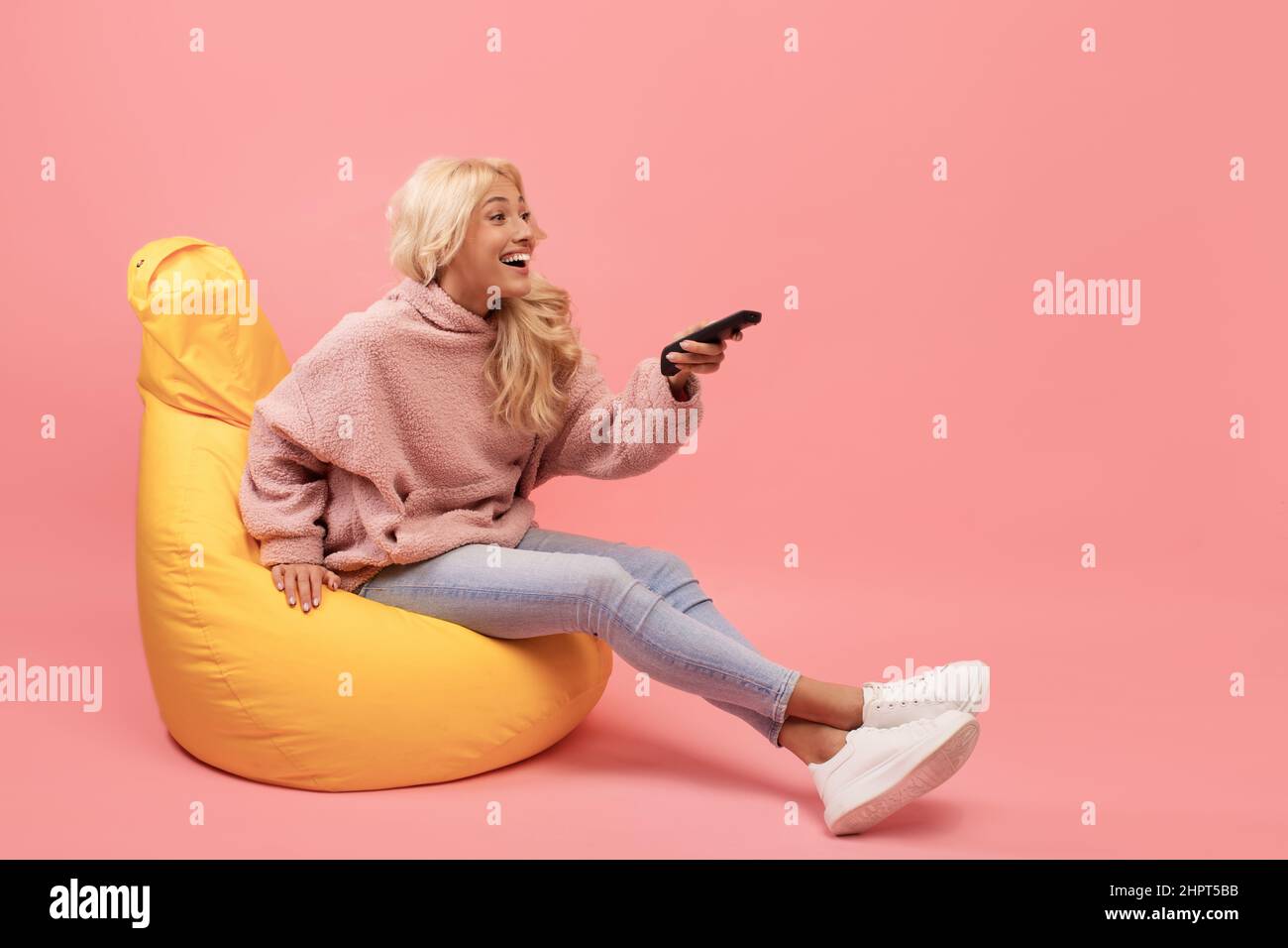 Excited lady with remote control sitting in beanbag chair and watching ...