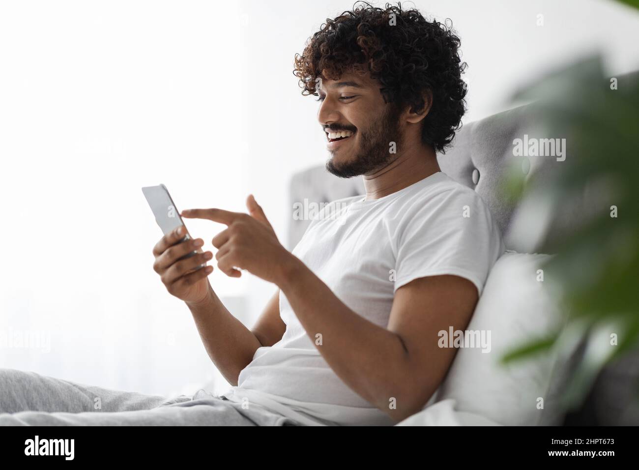 Positive dark-skinned guy scrolling in bed, using smartphone Stock Photo - Alamy