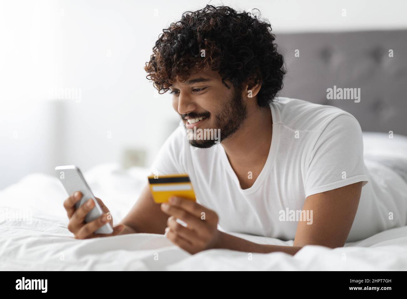 Dark-skinned guy laying in bed with credit card and smartphone Stock ...