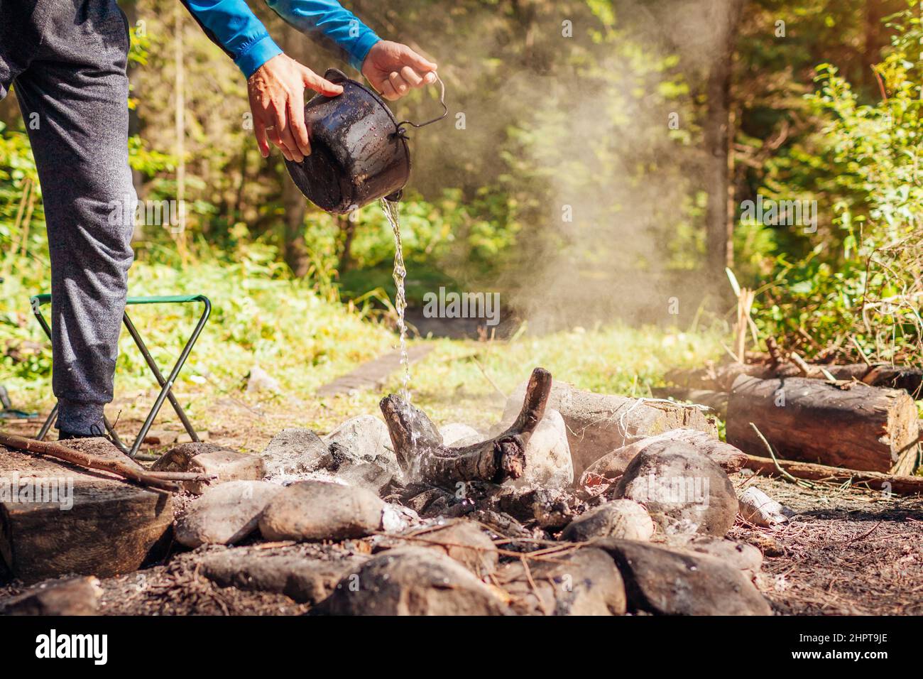 Man extinguishing campfire with water from cauldron in summer forest ...
