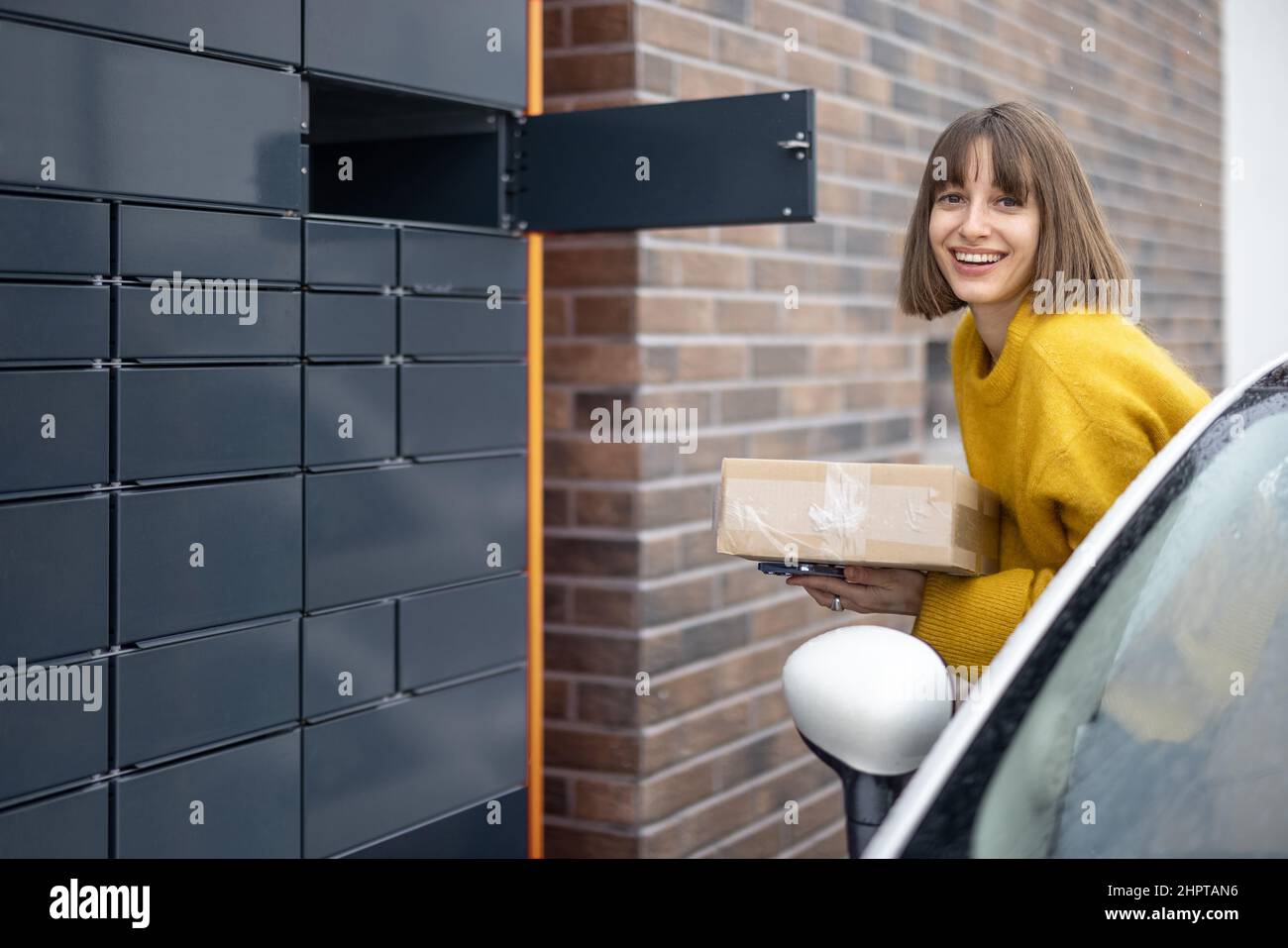 Portrait of a smiling woman looking out of the car window with parcel ...