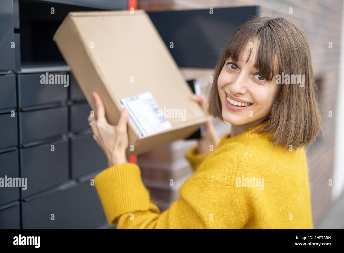 Woman getting parcel from cell of automatic post terminal outdoors ...