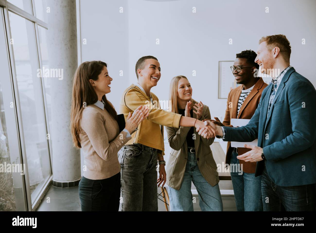 Memembers of young creative team shaking hands while working in the ...
