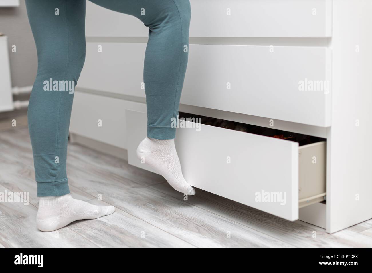 a female leg pushes a drawer of chest of drawers with her foot closing ...