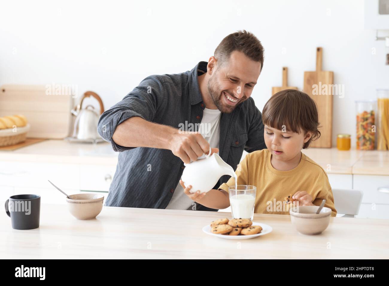 Happy caring father pouring fresh milk into glass, adorable little boy ...