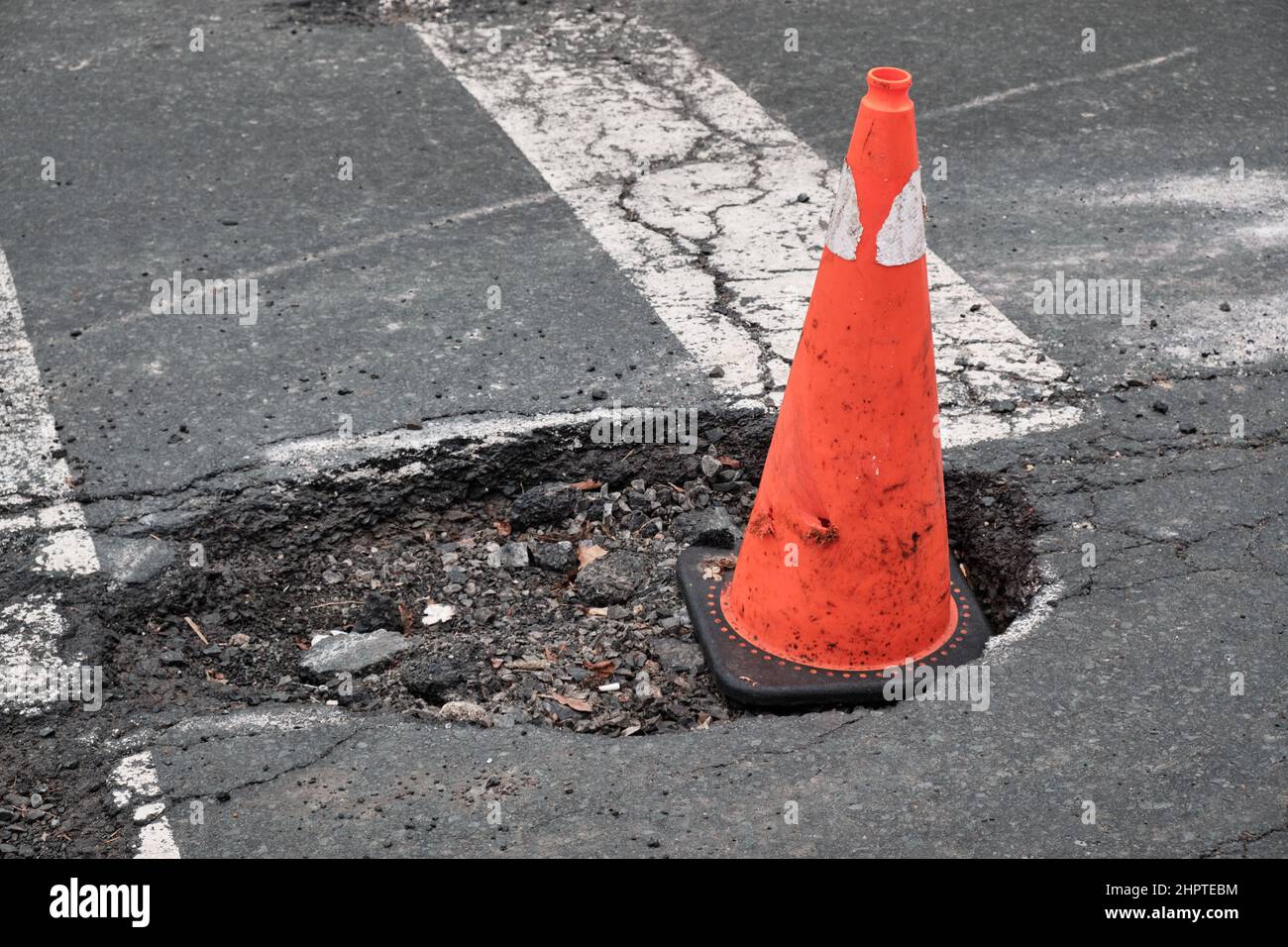 Large city street pothole at intersection with a warning orange cone in ...