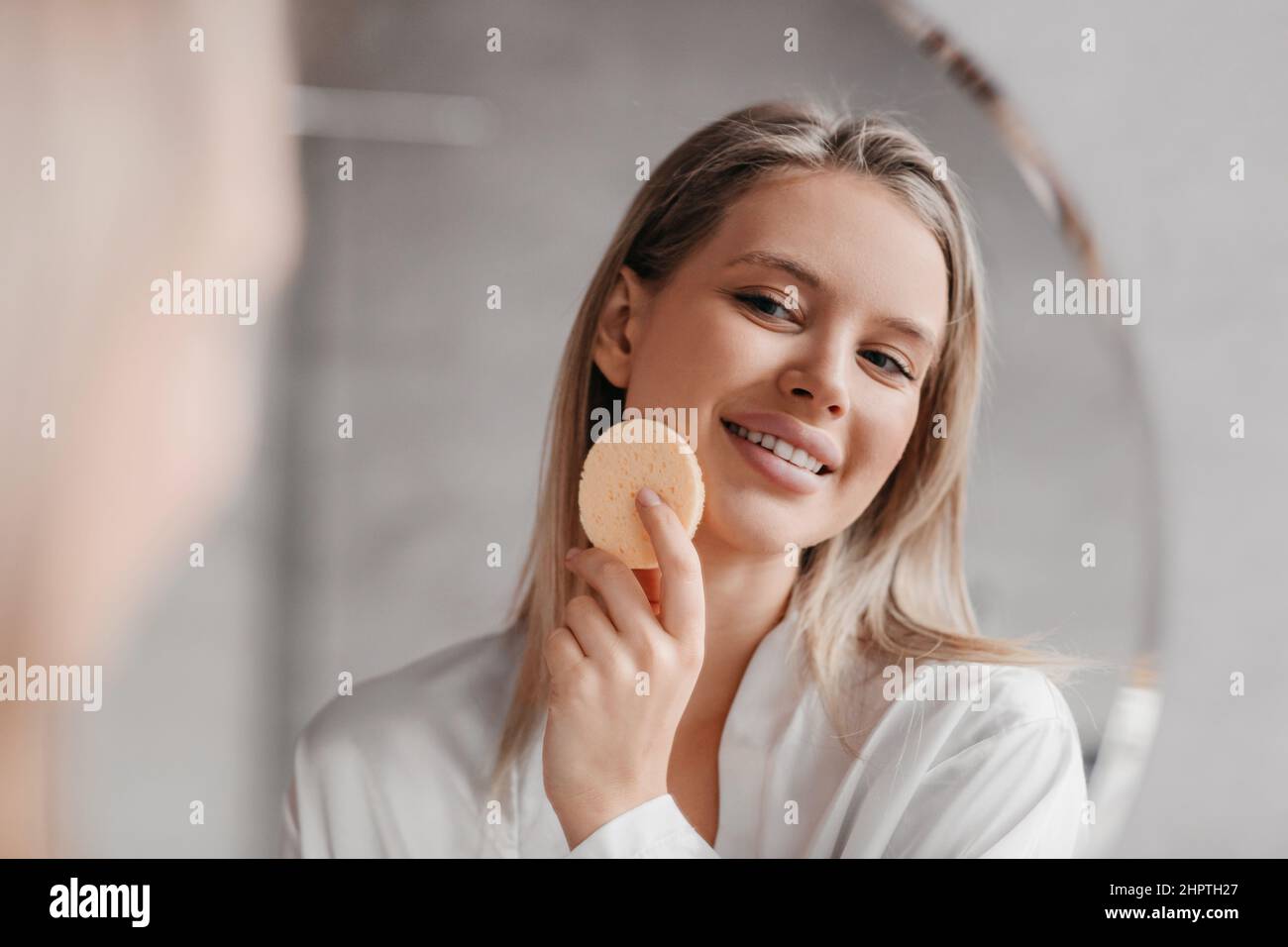 Attractive woman using cosmetic sponge while doing facial skincare ...