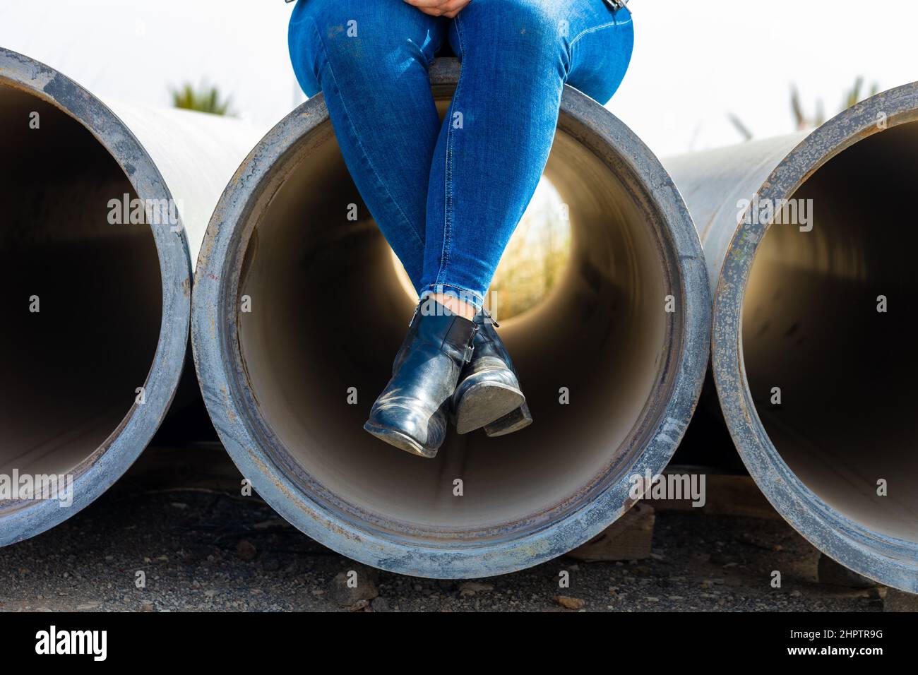 Feet of a woman sitting on the reinforced concrete pipes in the ...