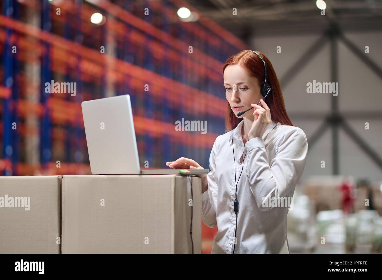 Woman in headset standing near laptop in warehouse Stock Photo - Alamy