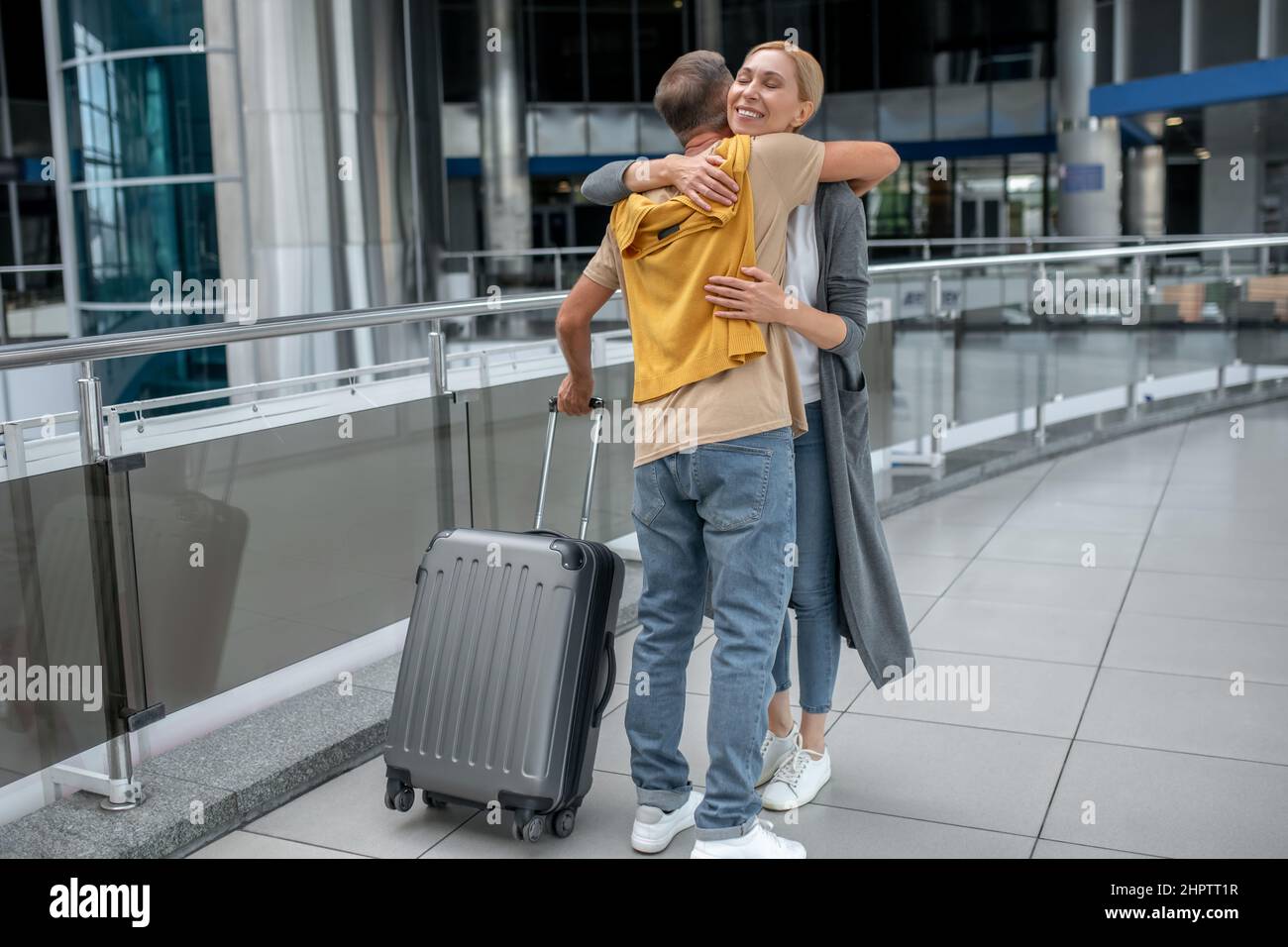 Woman hugging man with suitcase in terminal Stock Photo - Alamy
