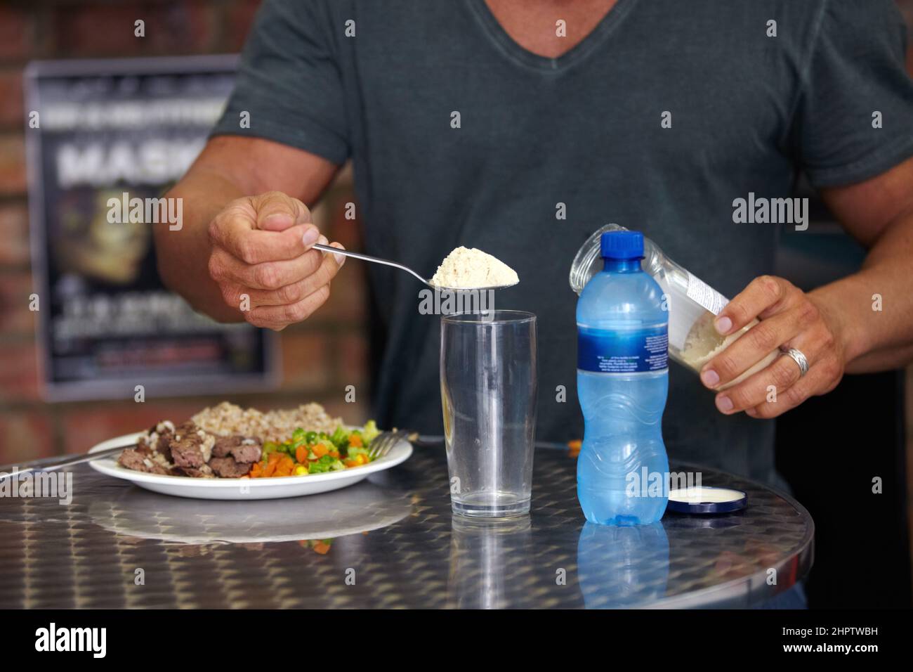 A bodybuilder adding supplements to his water while eating a protein ...