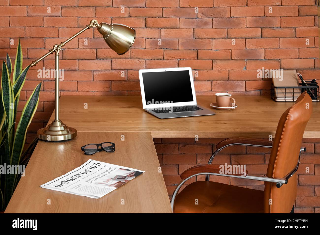 Modern workplace with laptop, lamp and newspaper near brick wall in ...