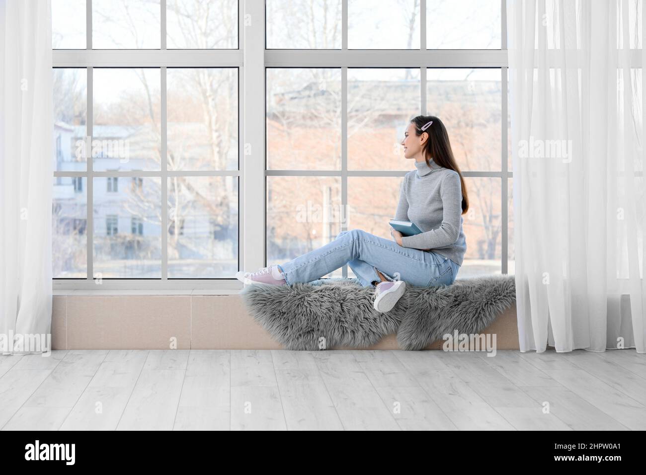 Pretty young woman with book sitting on window sill Stock Photo - Alamy