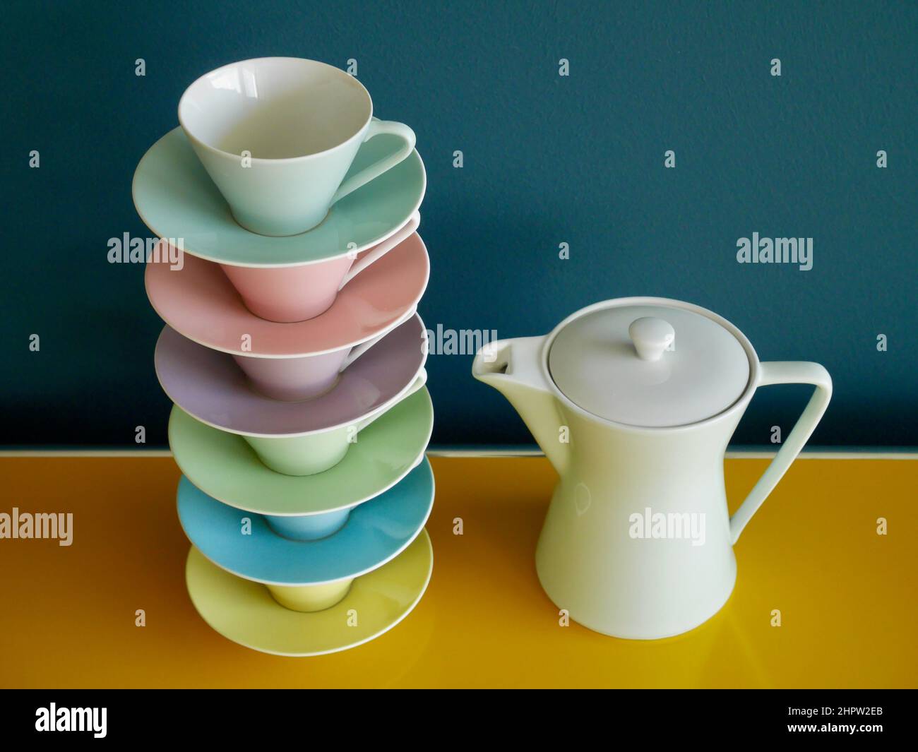 Stack of colorful vintage tea cups and tea pot on yellow table against ...