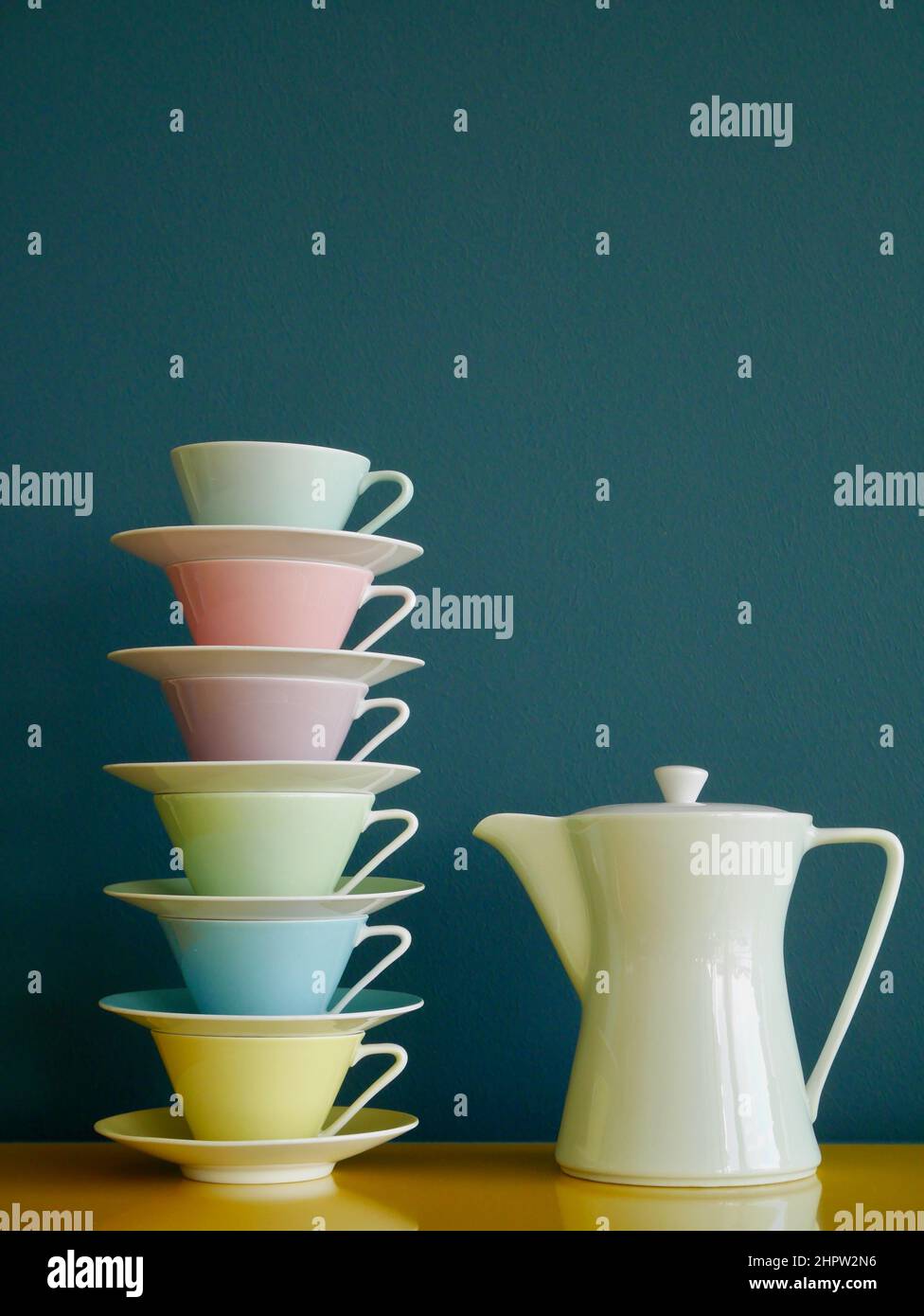 Stack of colorful vintage tea cups and tea pots on yellow table against ...