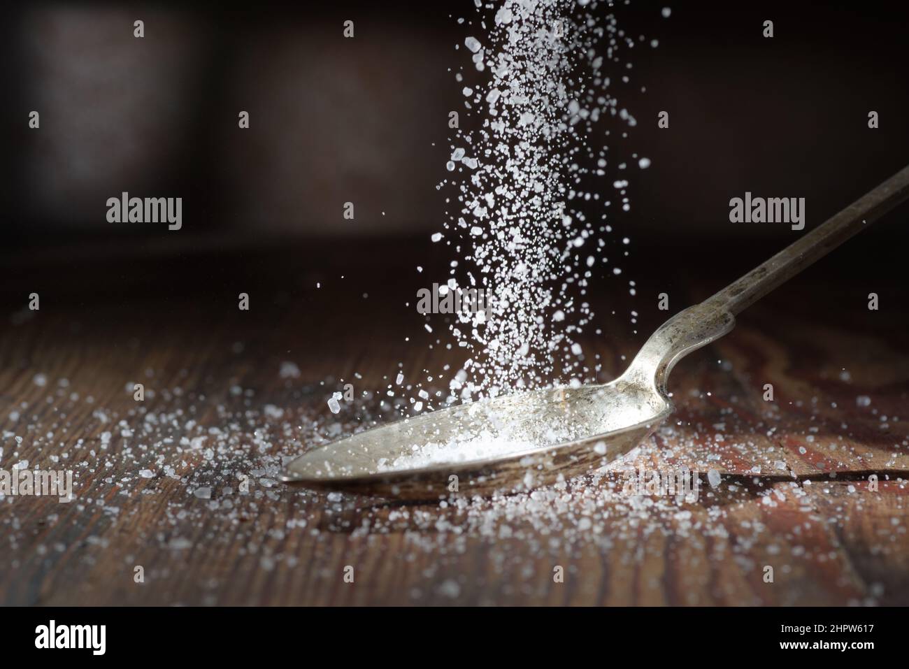 A falling of salt on a dark background, a spoonful of salt lies on top ...