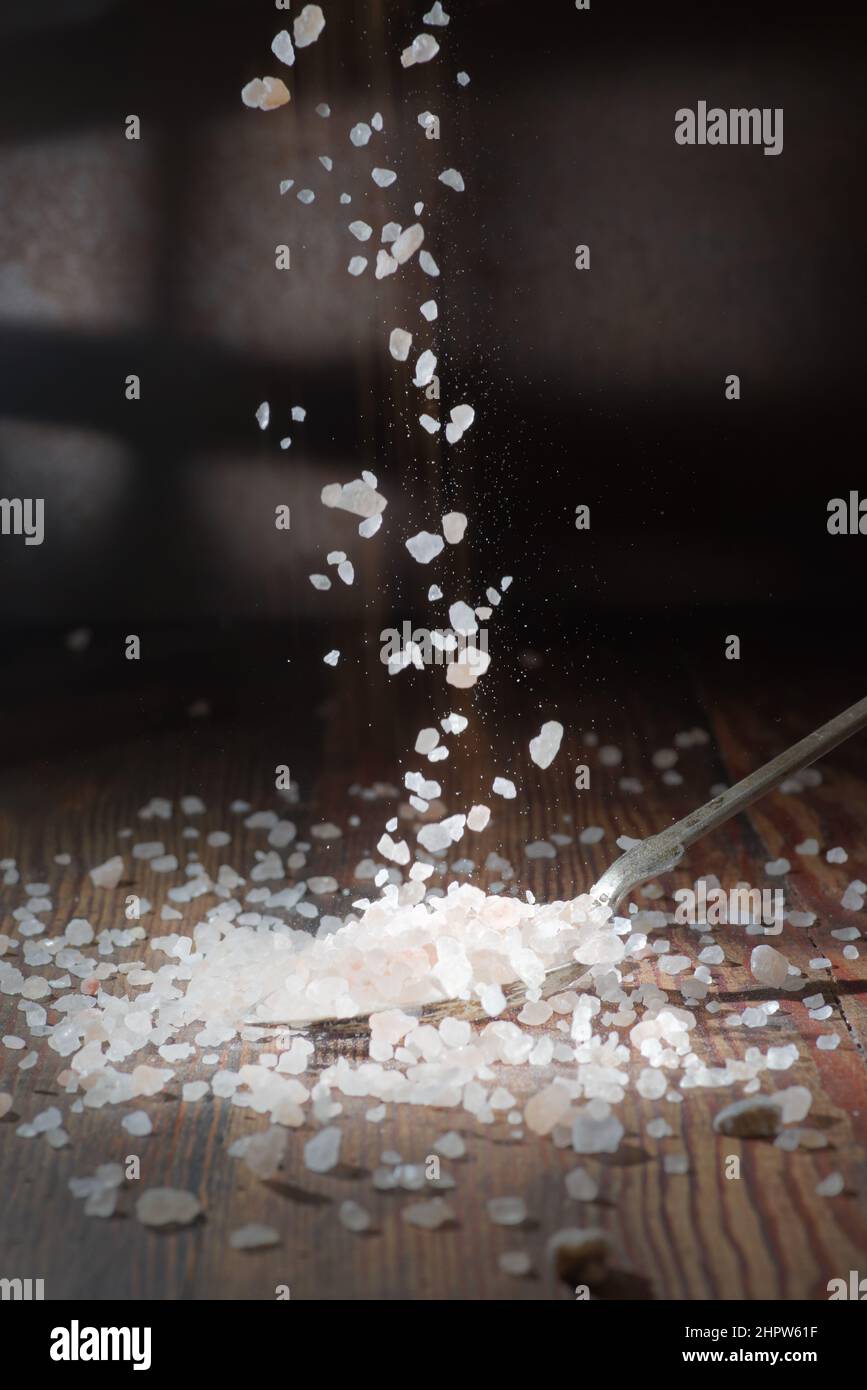 A falling of salt on a dark background, a spoonful of salt lies on top ...