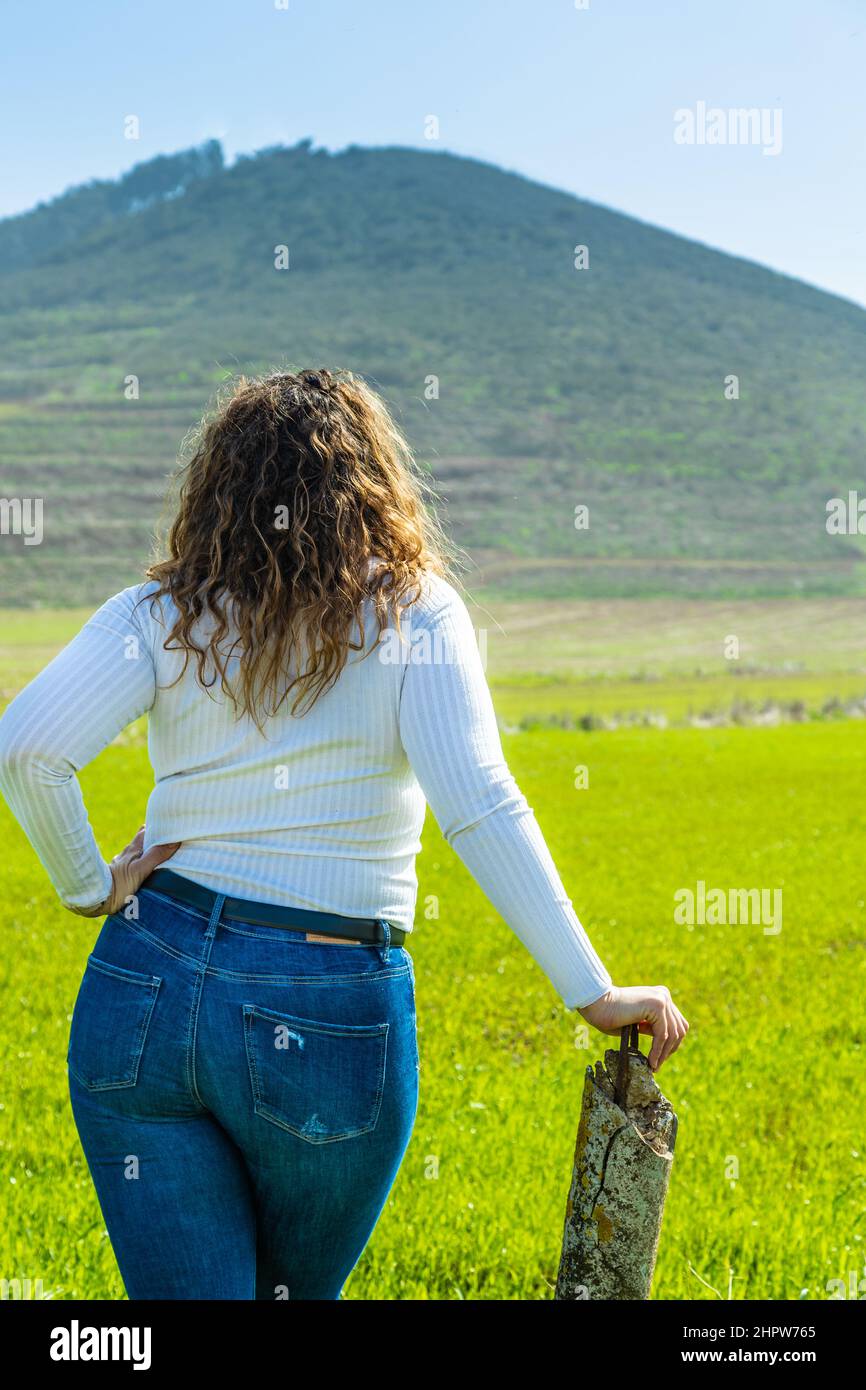 Back view of a woman leaning on a rusty stick, standing in the field ...