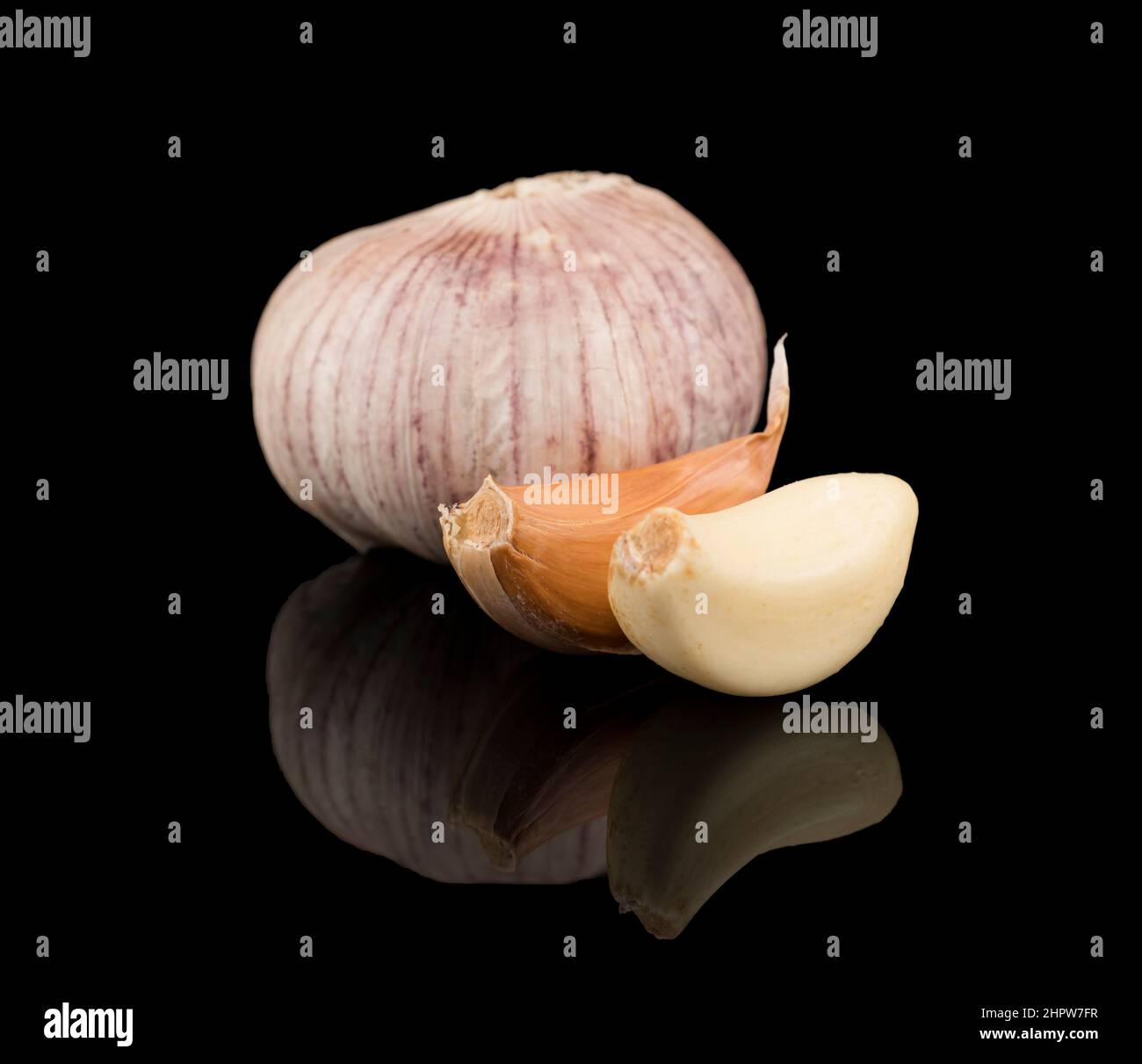 garlic, peeled and in the husk, on a black background, with reflection ...