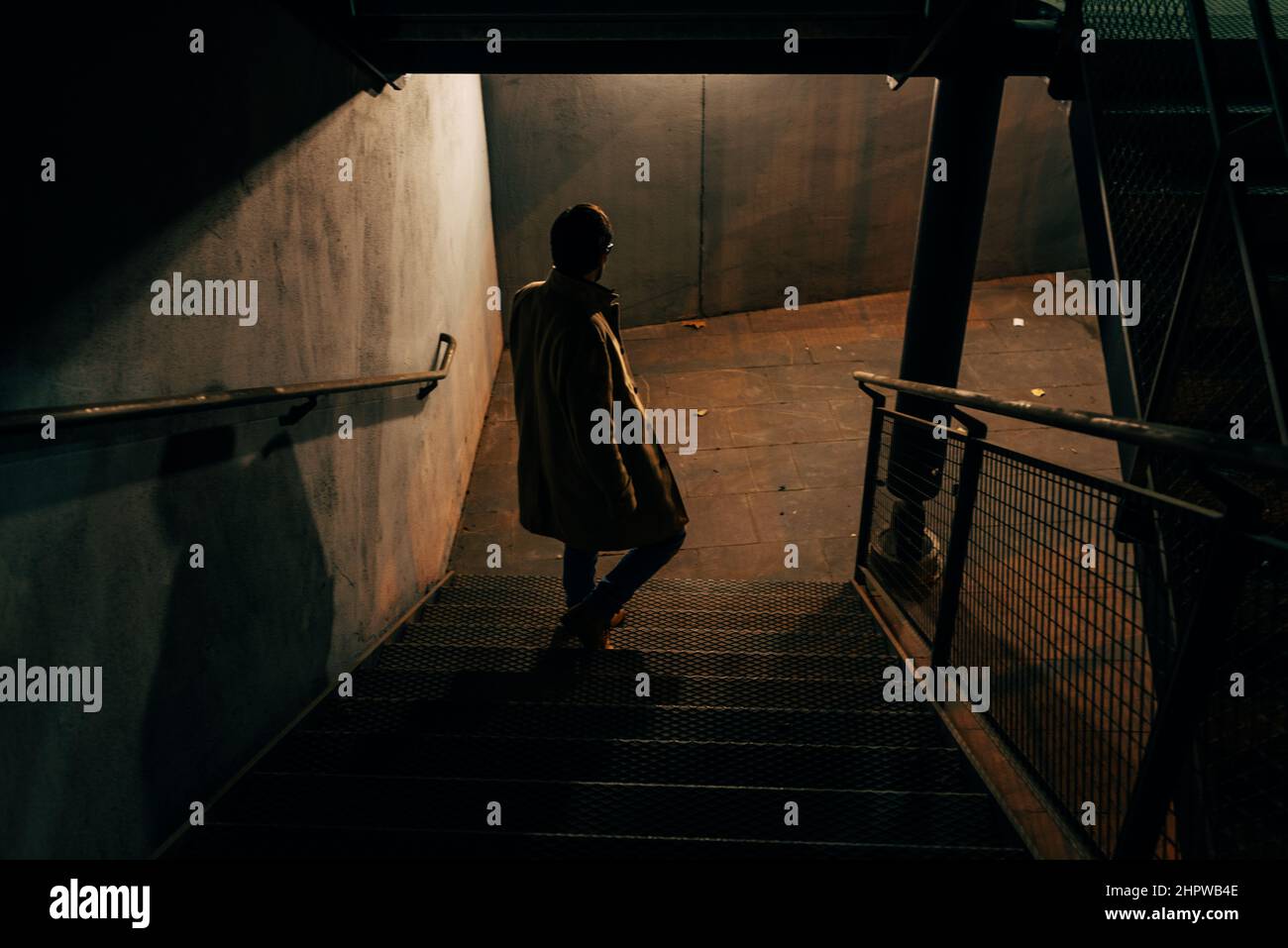Man descending metal emergency stairs in the shadows of the night ...