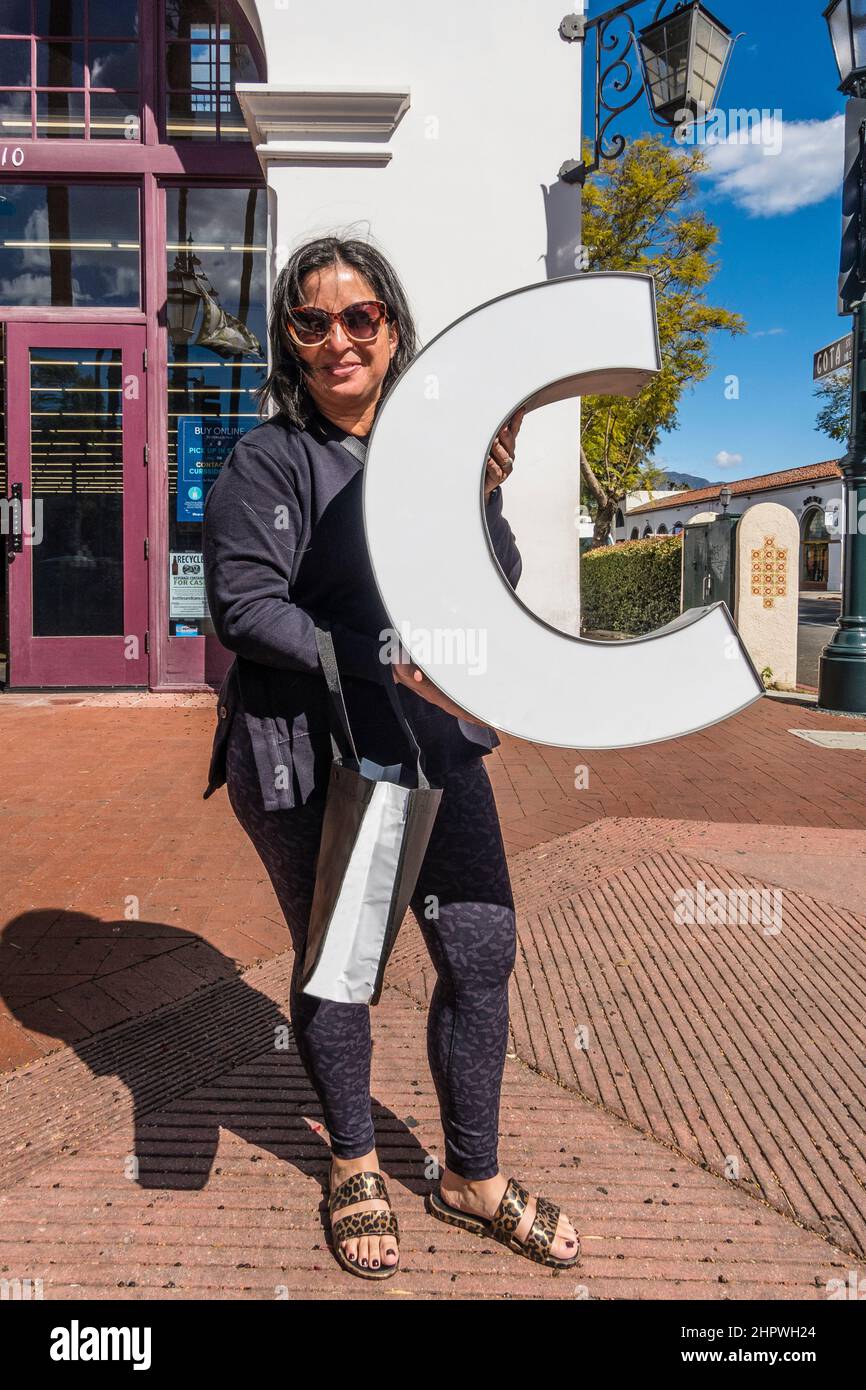 A woman holding on to a giant letter C while standing, facing forward ...
