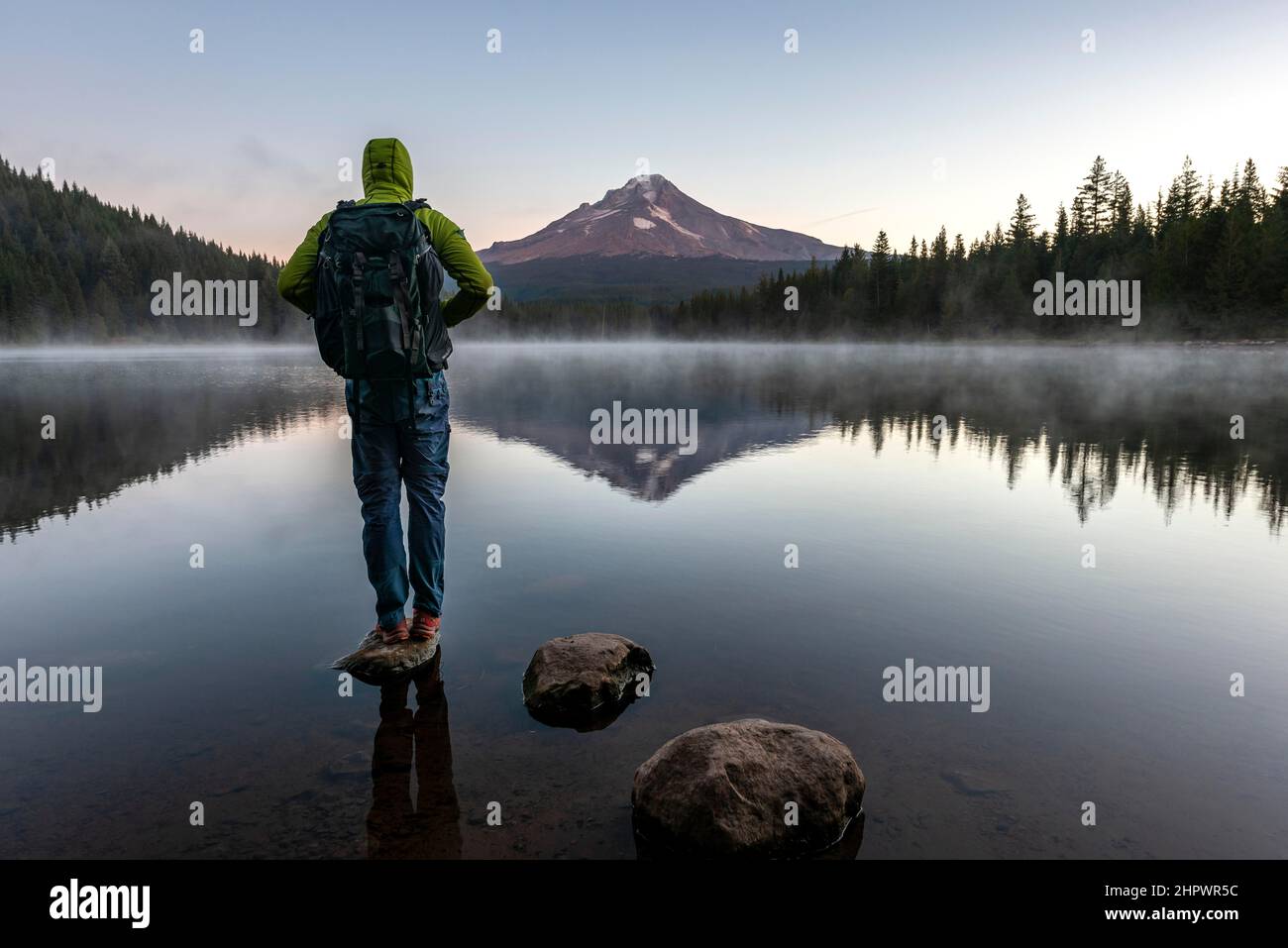 Young man standing on a stone, reflection of Mt. Hood volcano in ...