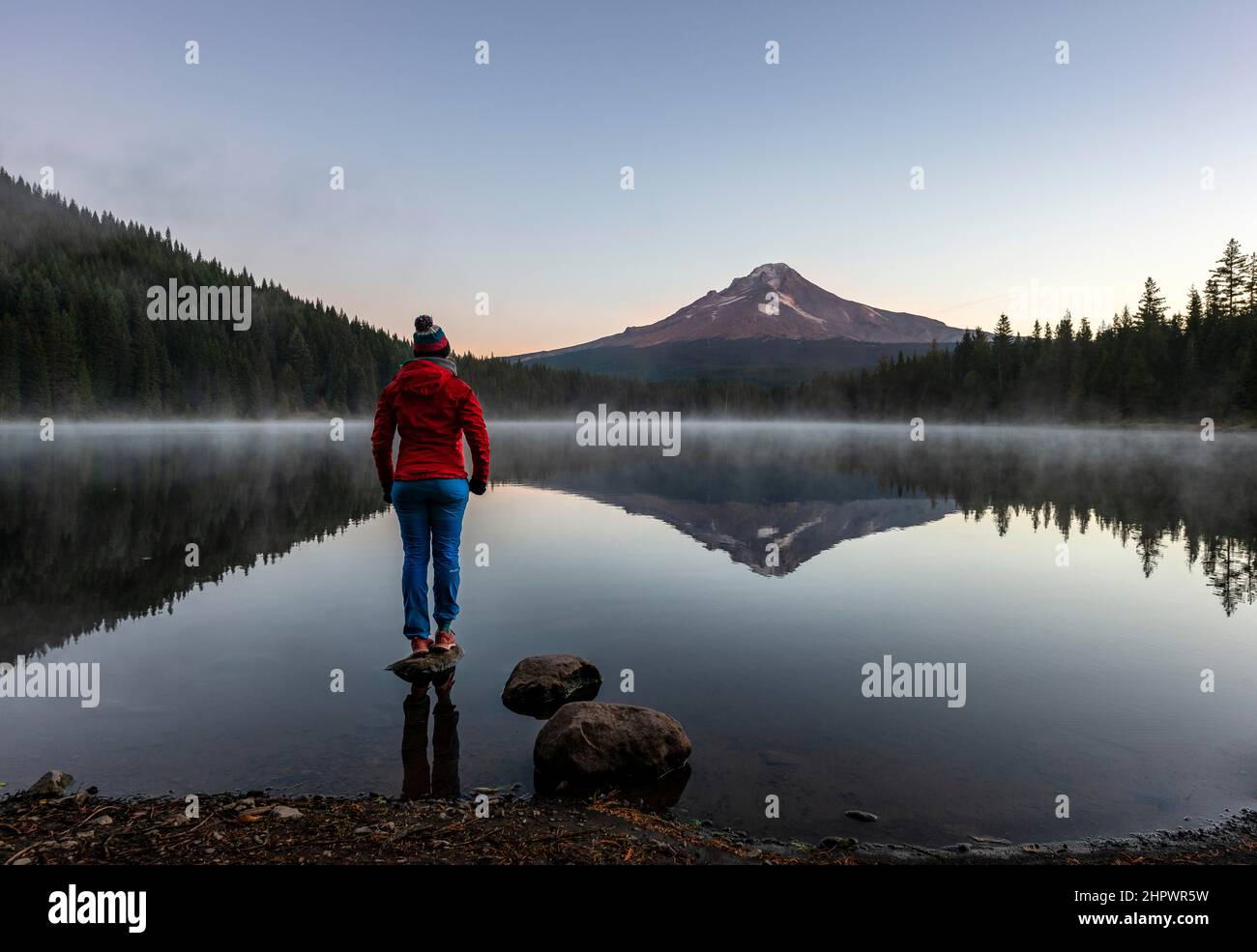 Young woman standing on a stone, reflection of Mt. Hood volcano in ...