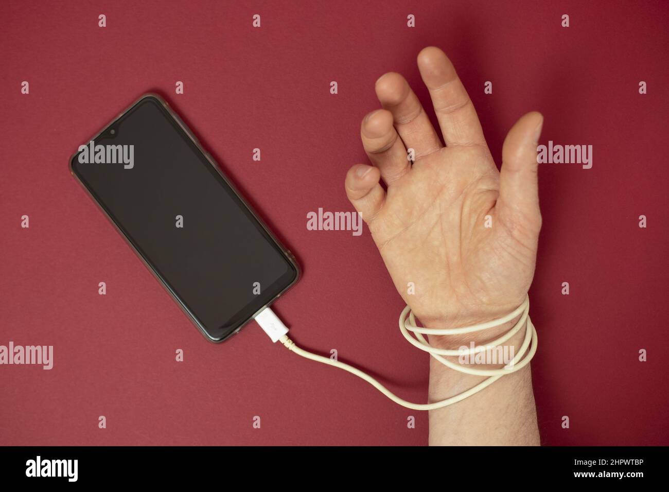 Hand tied to the phone by the charging cable on a red background Stock ...