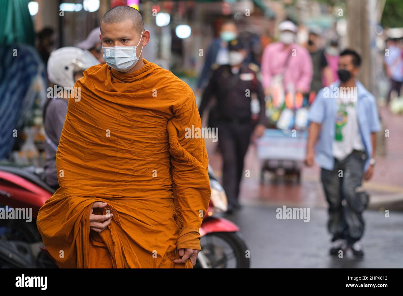 A young Buddhist monk walking a street in a busy market area in Bangkok ...