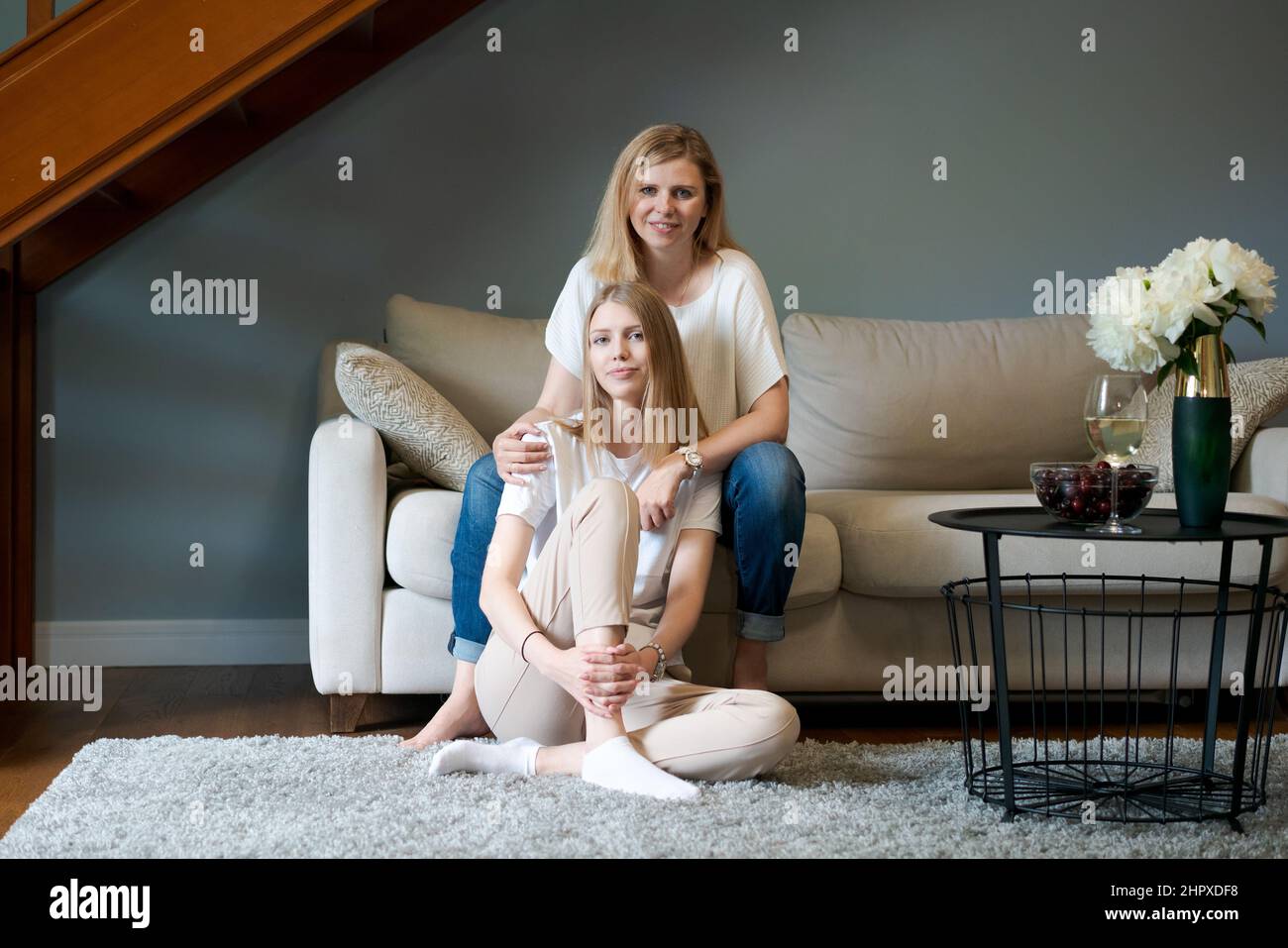 Portrait smiling family, middle aged mother and adult daughter hugging while sitting on cozy ...