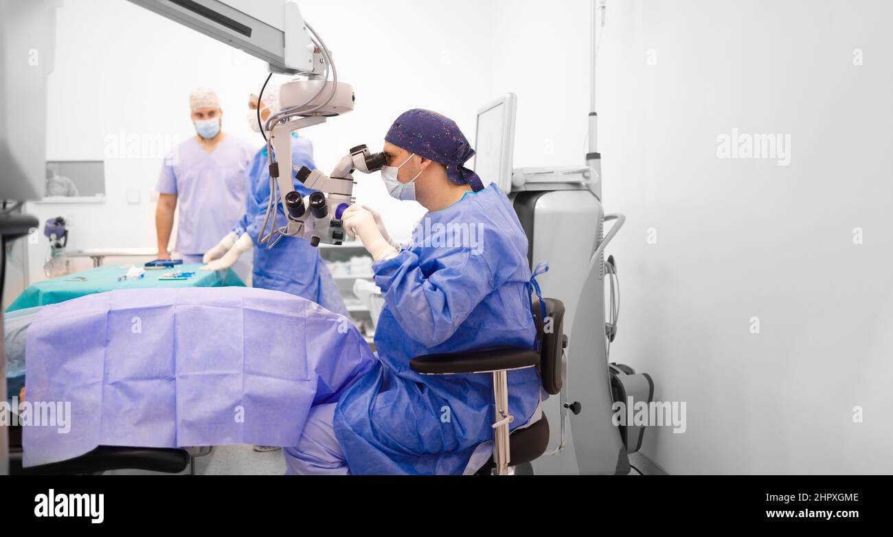 A surgeon looking through a surgical microscope and operating on his ...