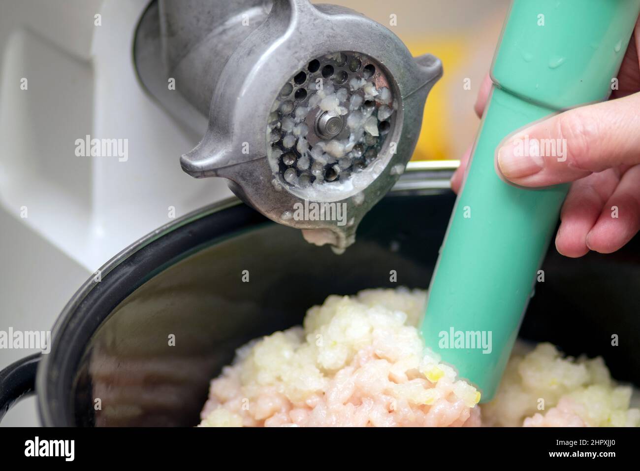 closeup of a mincer and a hand with plunger mixing minced meat with ...