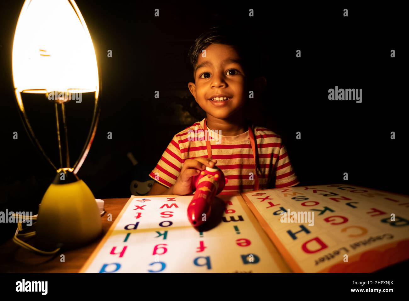 A boy learning the English alphabet using a charger lamp In the evening ...