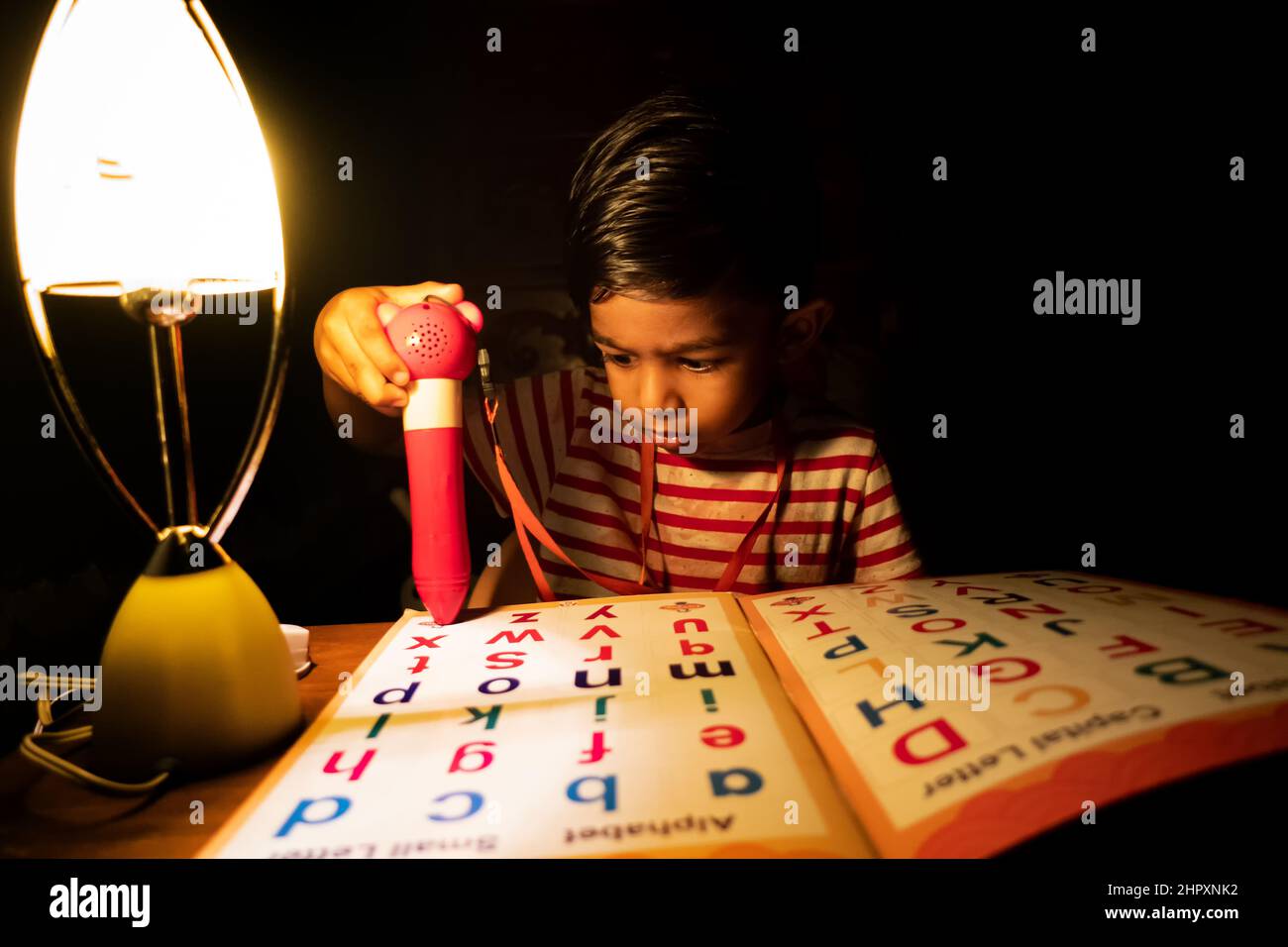 A boy learning the English alphabet using a charger lamp In the evening ...