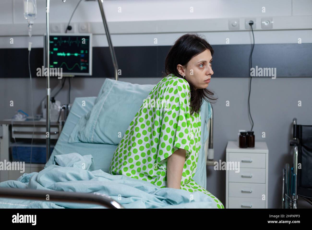 Patient with illness feeling depressed sitting on bedside looking into ...