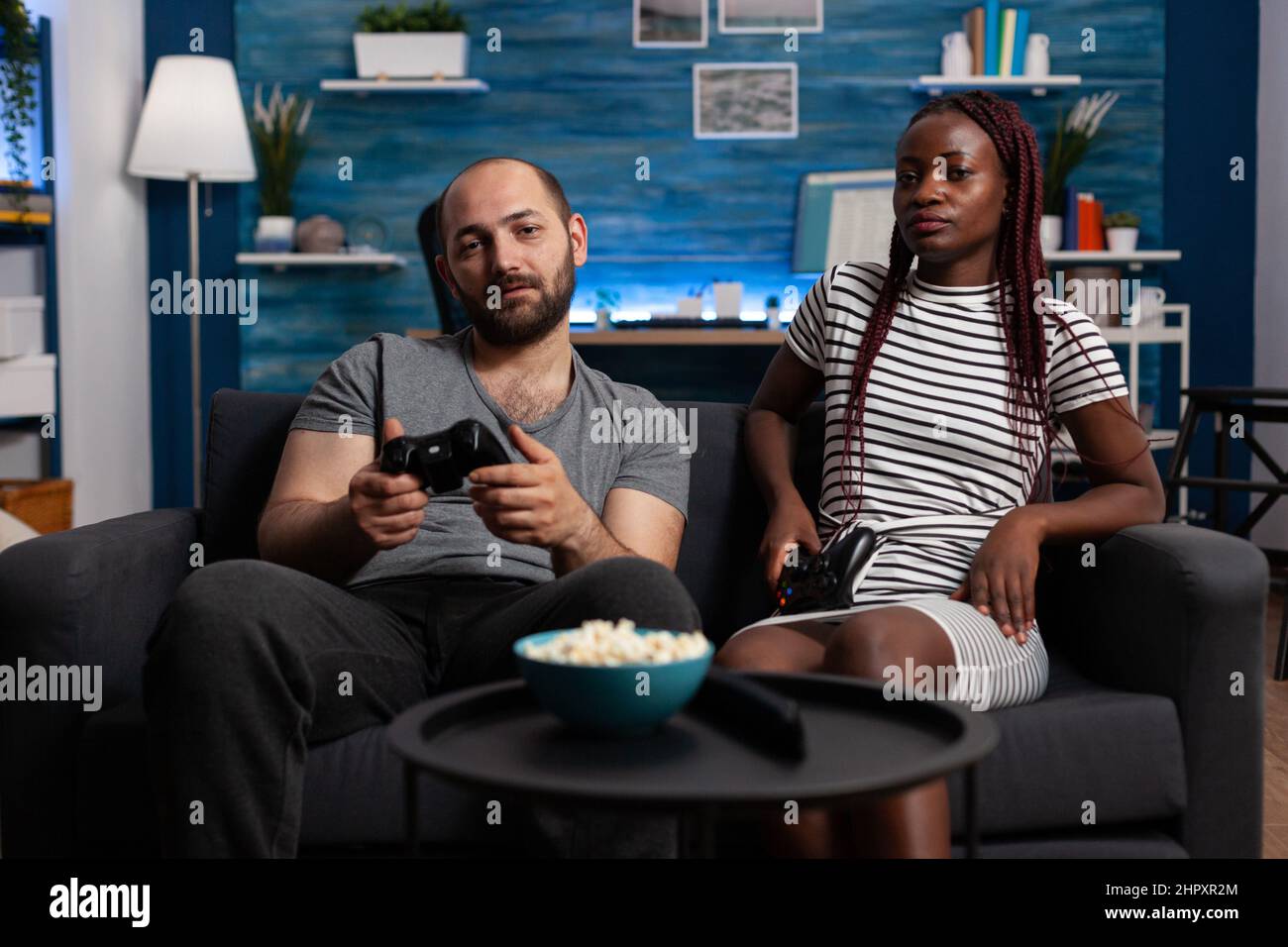 Multiethnic adult couple playing video games on console sitting on ...