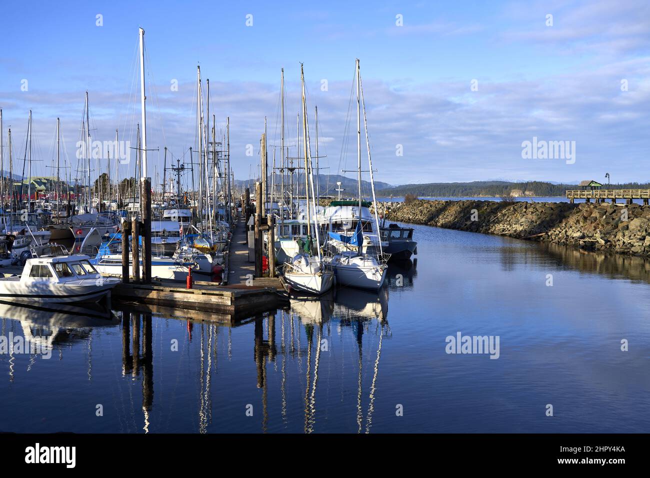 White pleasure boats tied up to a wooden dock beside a rocky breakwater ...