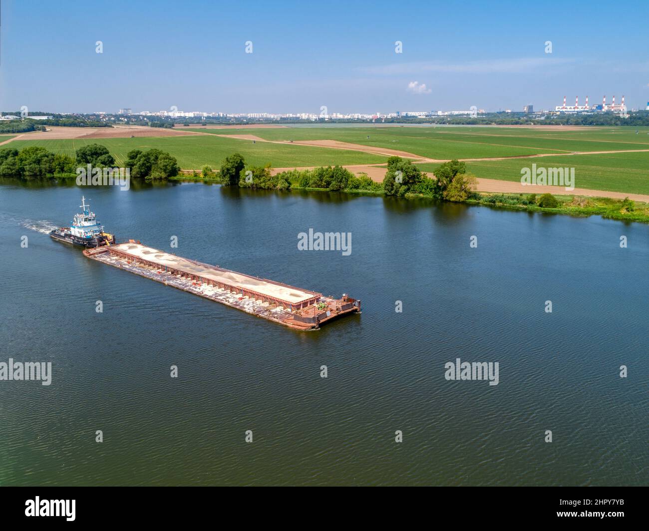 Small towboat pushes barge along calm water past fields Stock Photo - Alamy